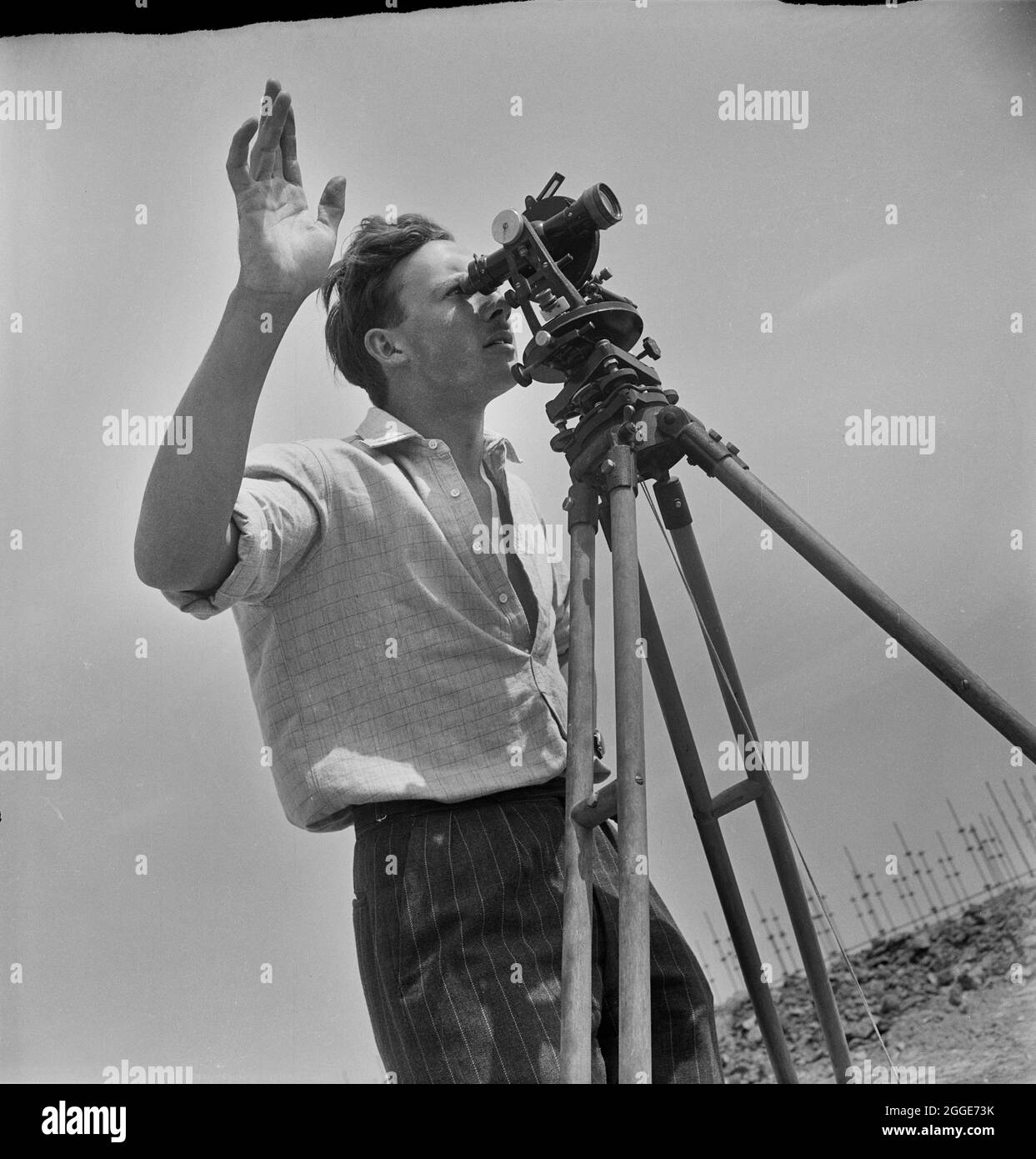 A man using a mounted theodolite to survey the construction site of an ...