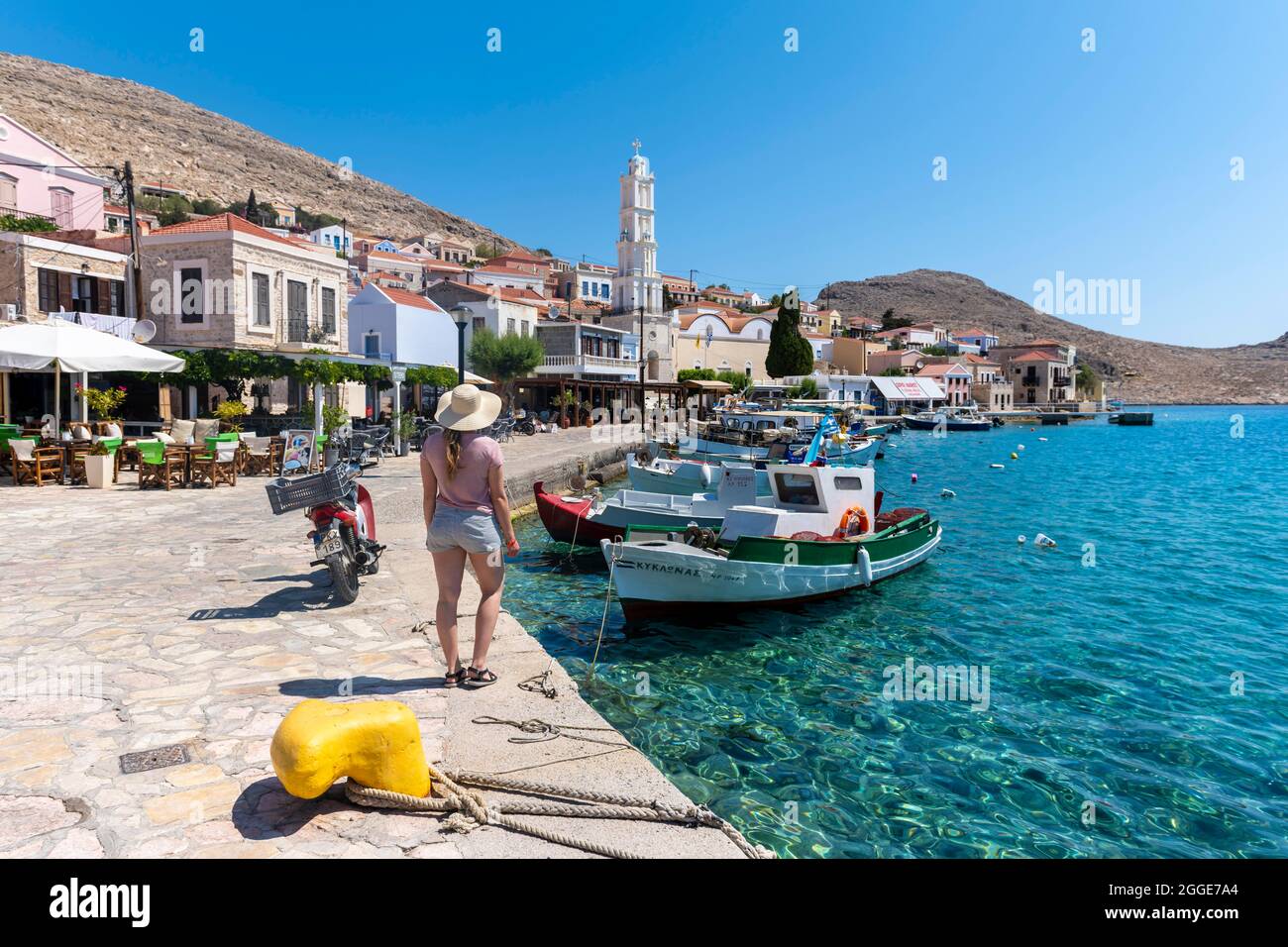 Tourist with sun hat, fishing boats in Halki harbour with turquoise ...