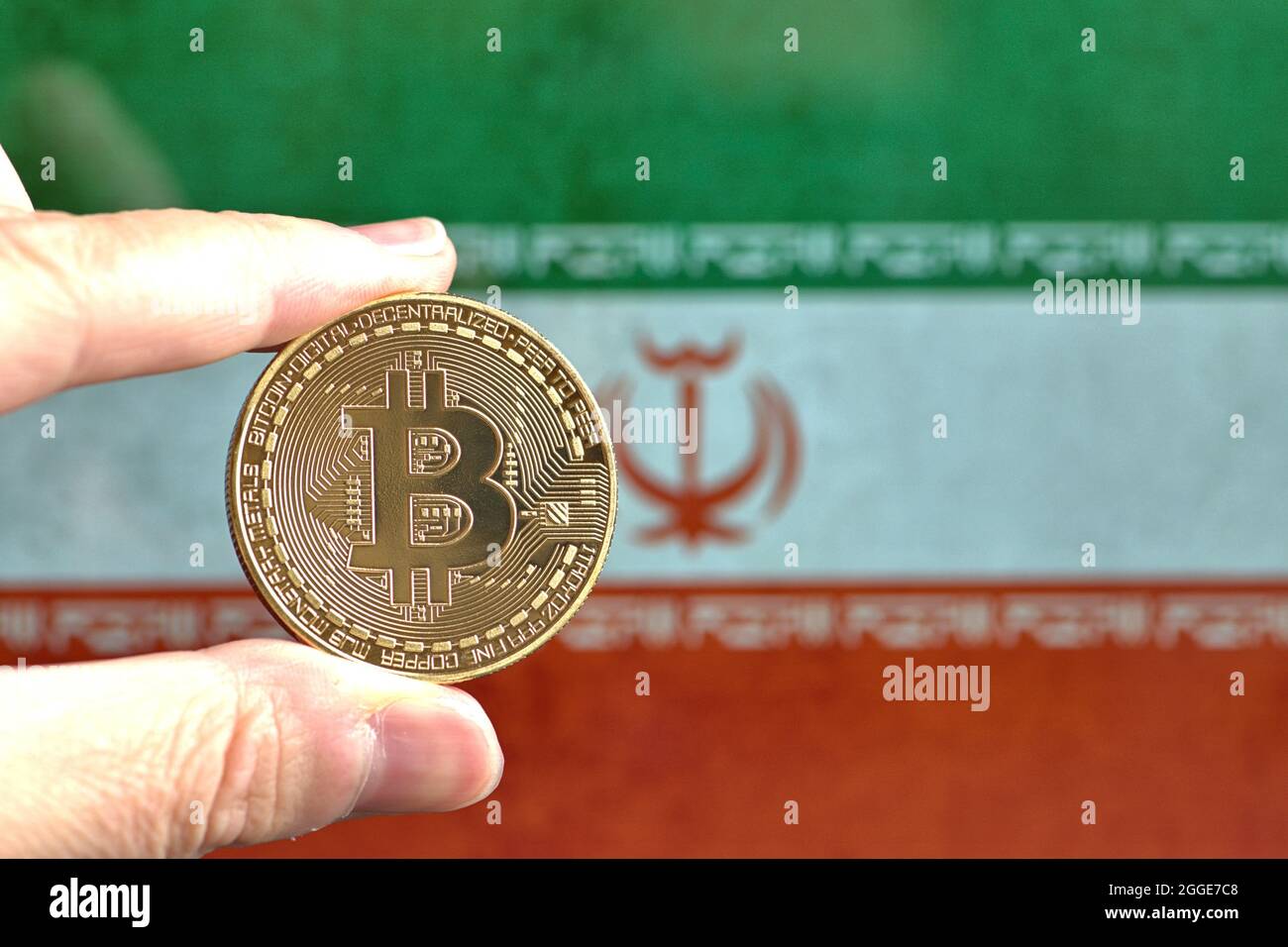 A Bitcoin coin held by a hand in front of a representation of the ...