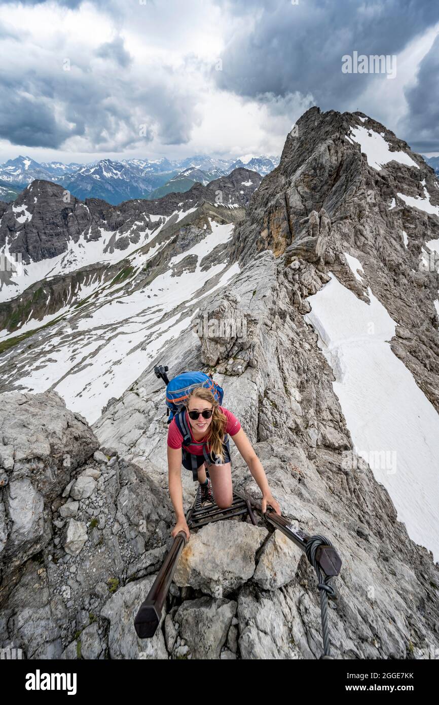 Hiker climbing metal ladder on rock, climber on ridge path with snow ...