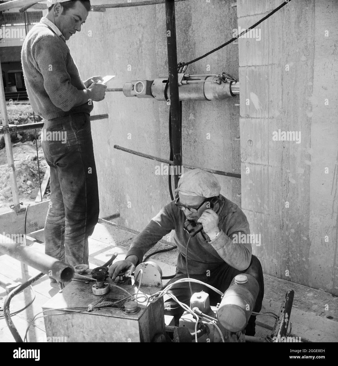 Two workers carrying out post-tensioning of stressing cables running ...