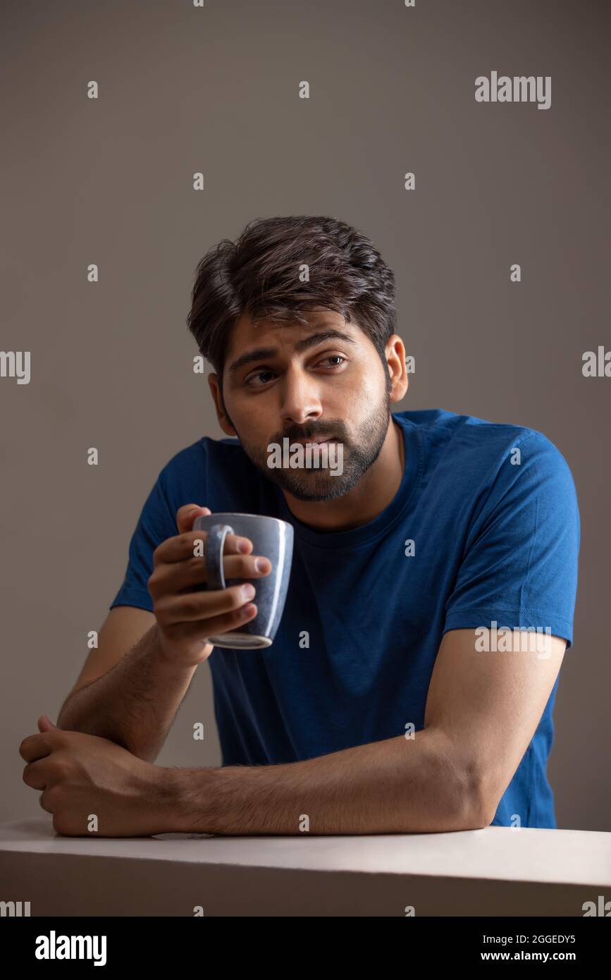 A YOUNG MAN SITTING AND THINKING WHILE HOLDING COFFEE MUG Stock Photo ...