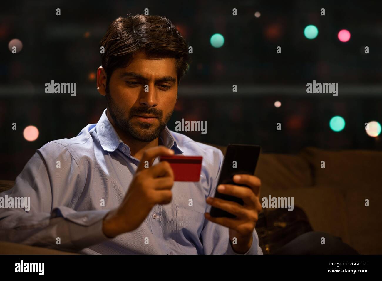 A YOUNG PROFESSIONAL CAREFULLY LOOKING AT DEBIT CARD WHILE DOING ONLINE ...