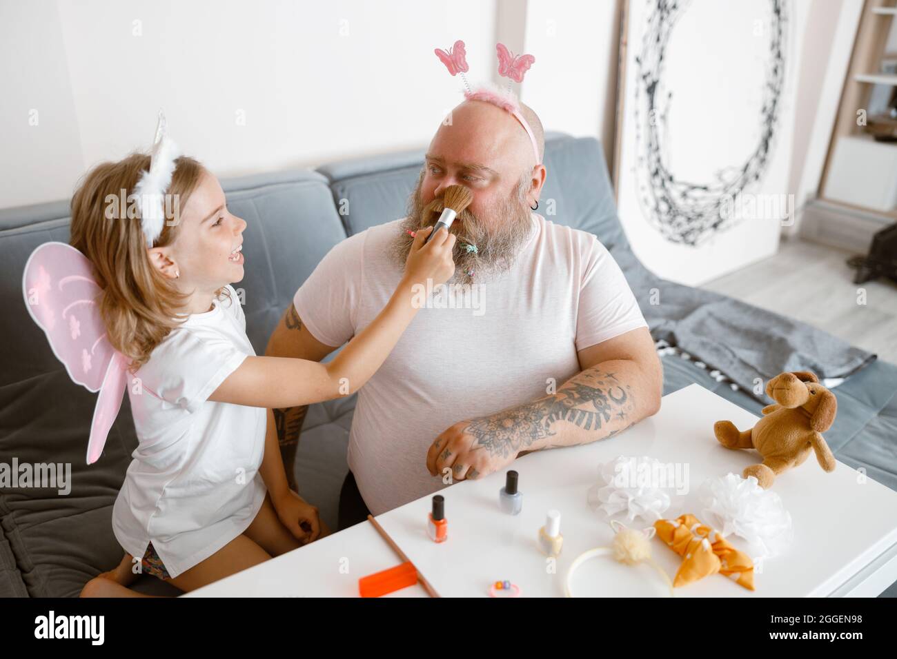 Joyful child applies powder onto father face playing beauty salon at ...
