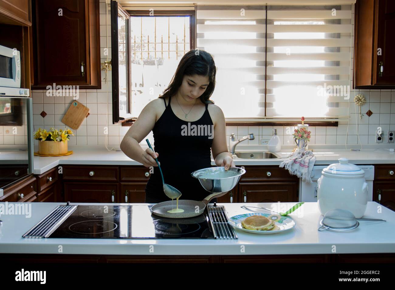 young girl is cooking pancakes for breakfast in the kitchen of her home ...