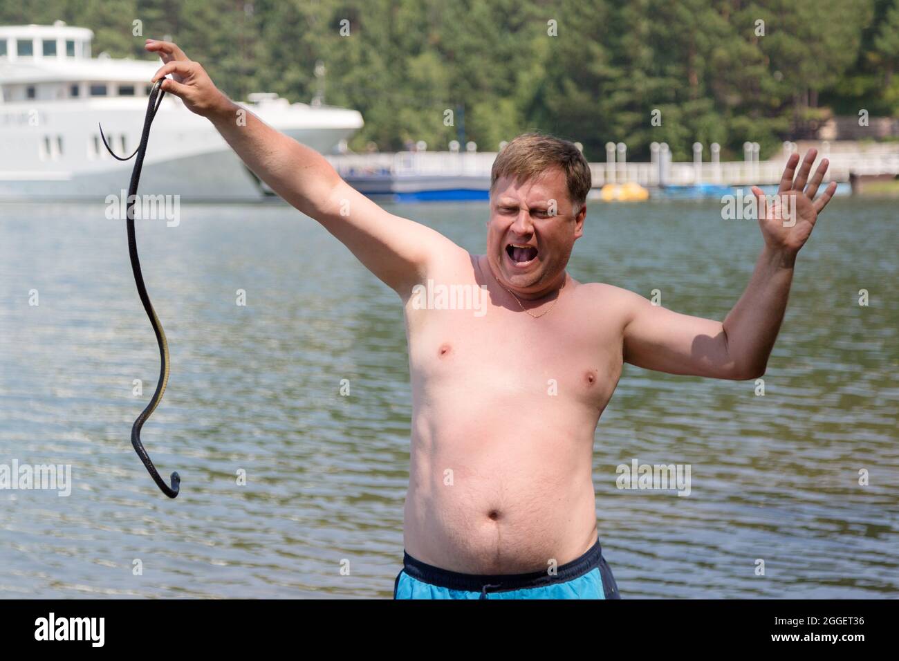 Frightened man standing in water holding a poisonous snake, shouting ...