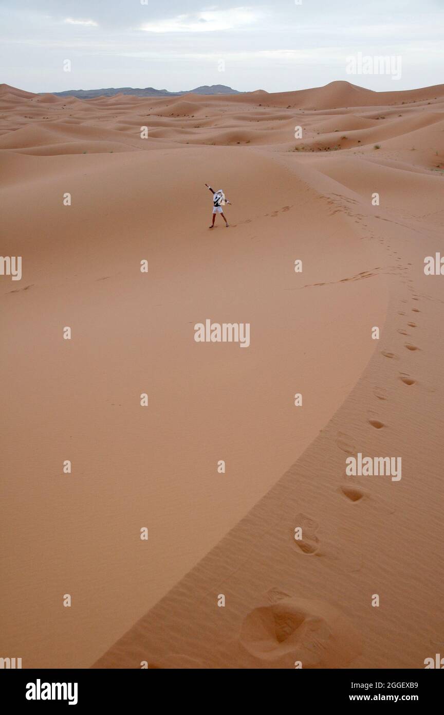 Aerial view shot of a young male in a white cloth walking in a desert ...
