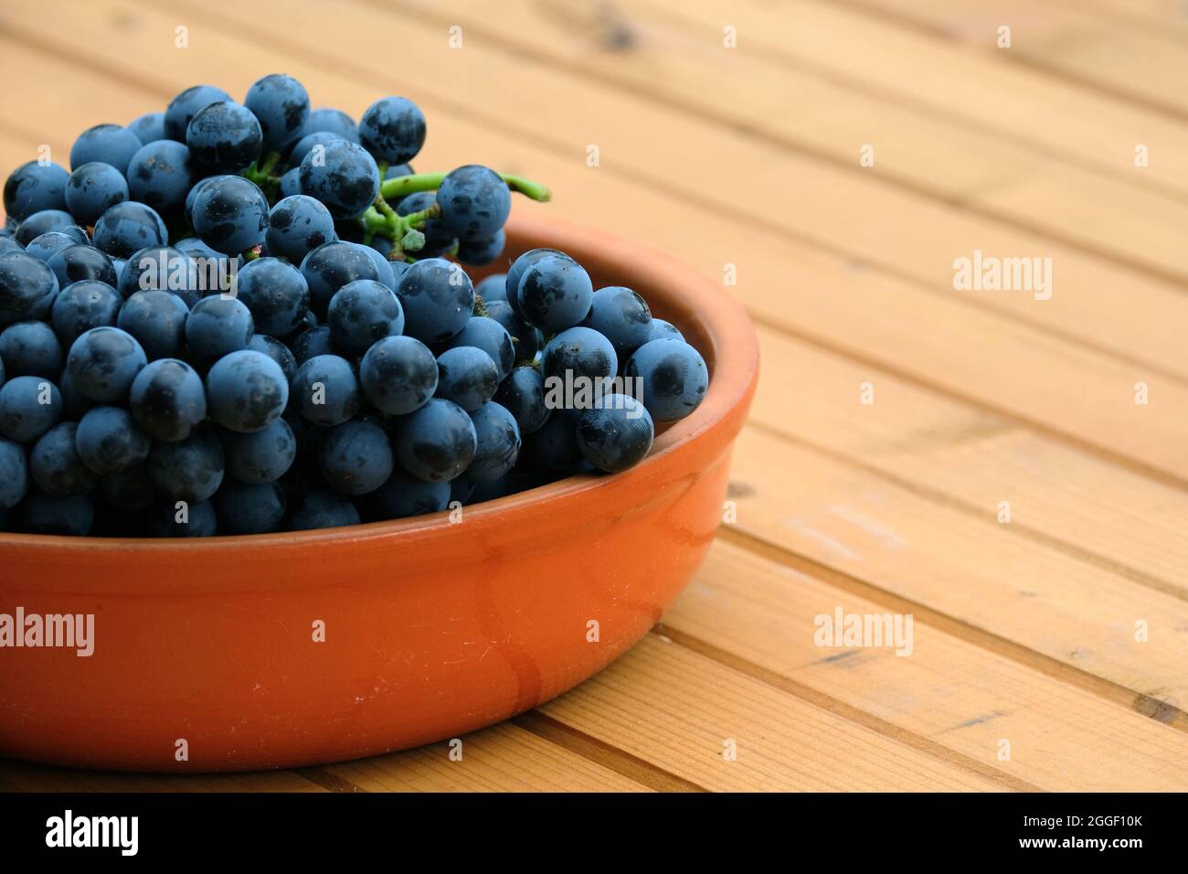 Lot of ripe red grape berries on bunch in brown round bowl on wooden ...