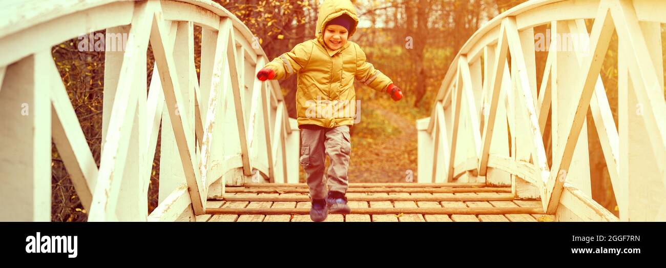 little happy four year old kid boy in autumn clothes runs and jumps on ...