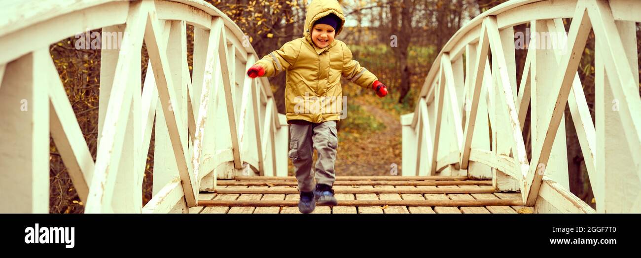 little happy four year old kid boy in autumn clothes runs and jumps on ...