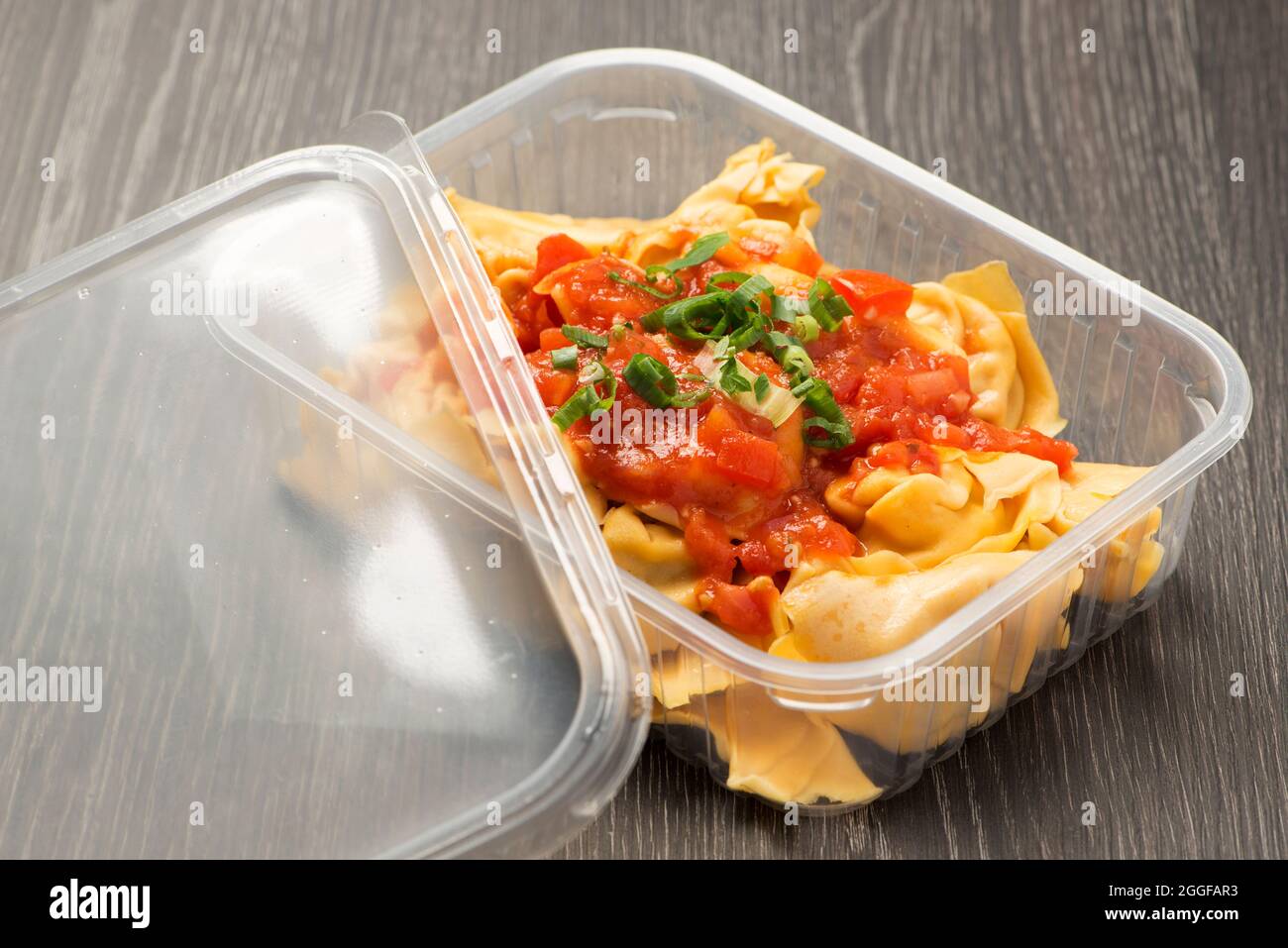 plastic lunch box with ravioli and tomato sauce sprinkled with chives ...