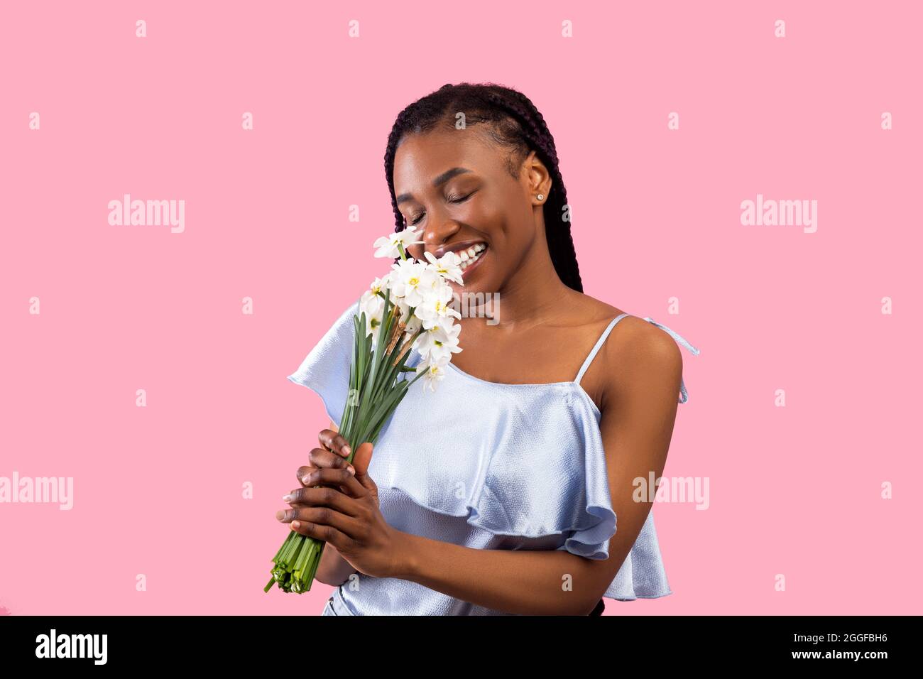 Millennial black lady smelling bunch of daffodils over pink studio ...