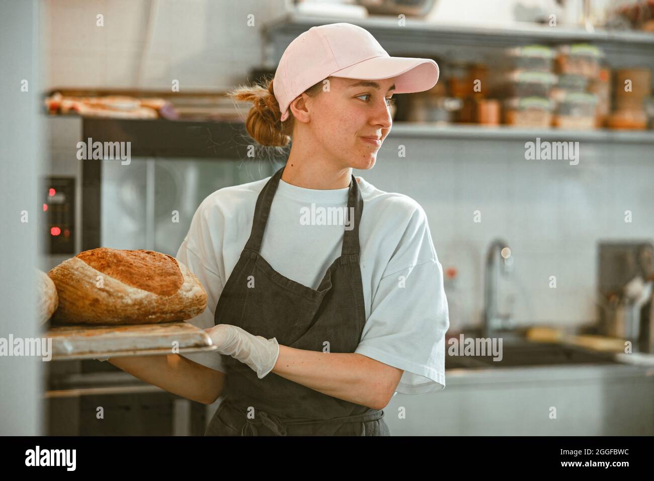 Cheerful lady holds tray with bread standing in craft bakery workshop ...