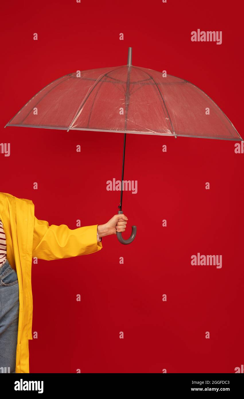 Woman in raincoat holding opened transparent umbrella against red ...