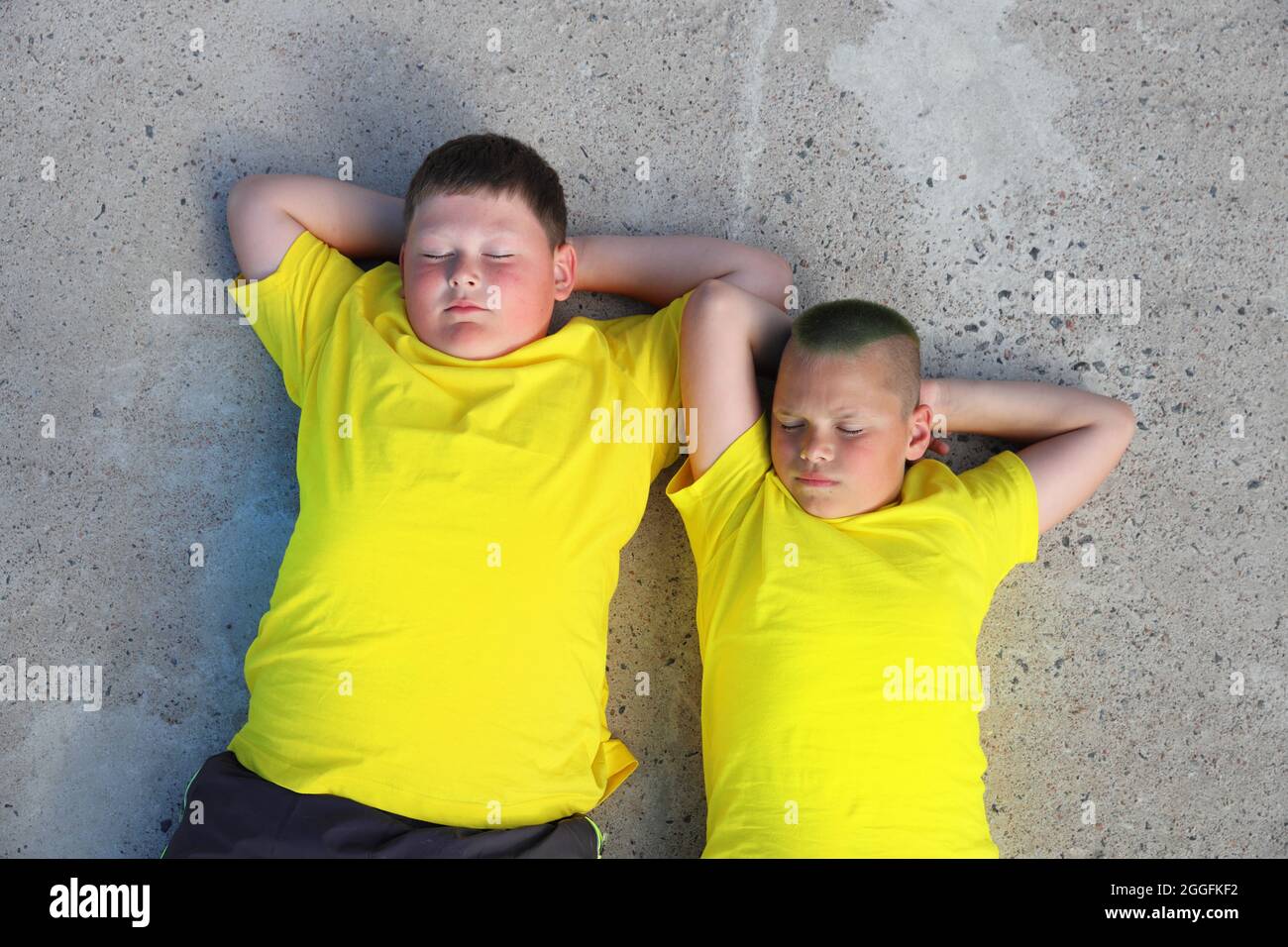 two boys in yellow T-shirts lie on the floor with their hands behind ...