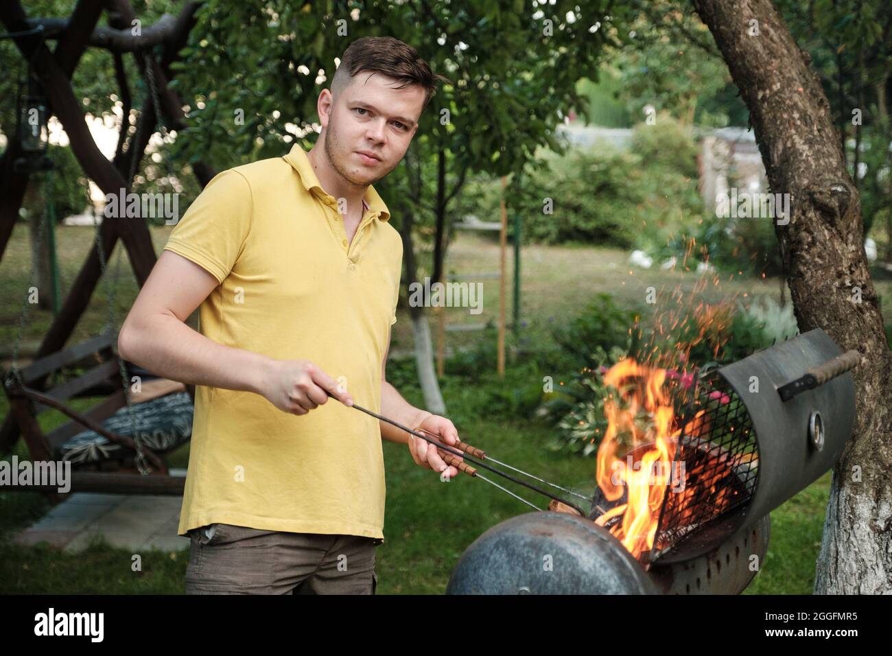 Young man putting firewood in mangal. Handsome athlete male builds a ...