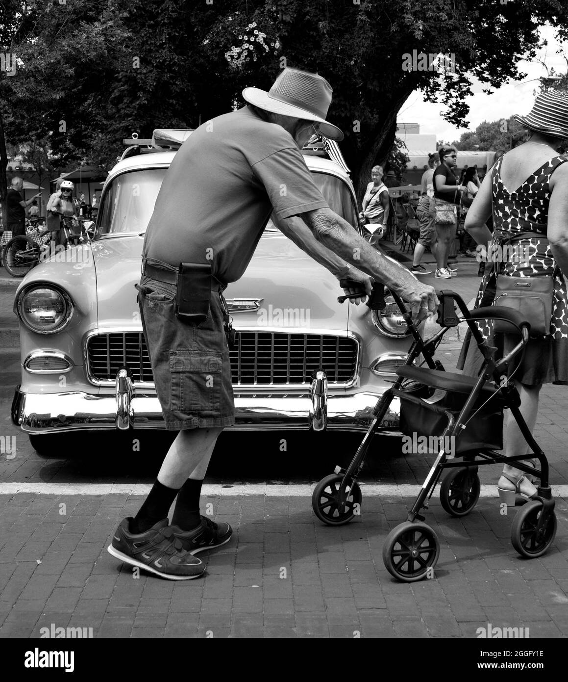 An elderly man using a mobility walker with wheels walks past a 1956 ...