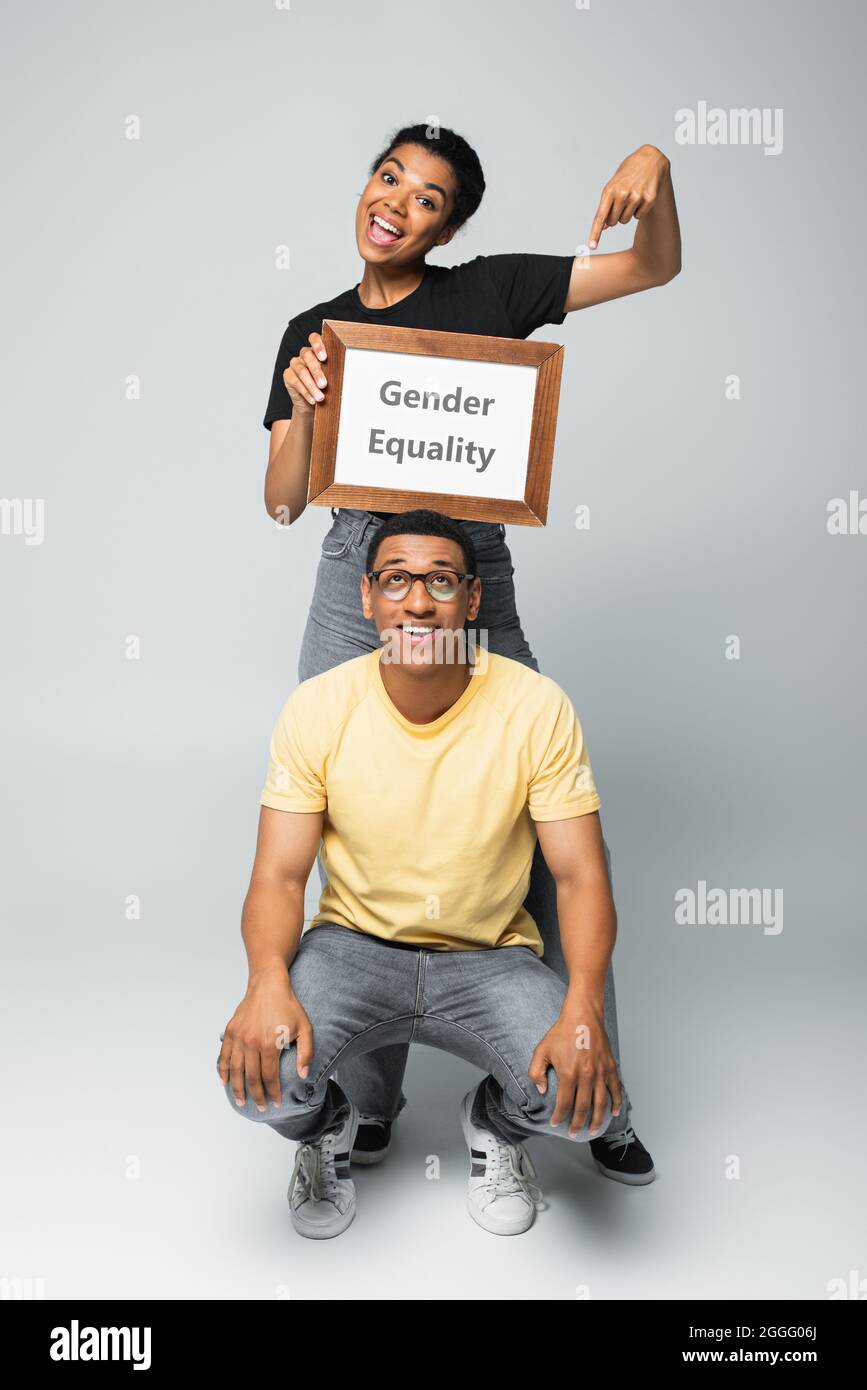 full length of cheerful african american woman pointing at placard with ...