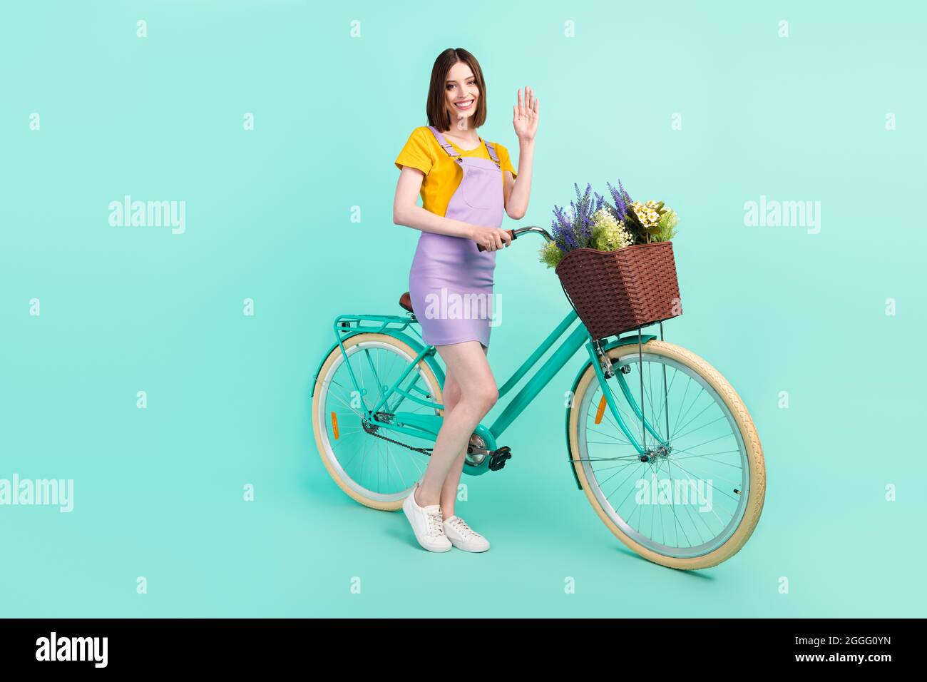 Full body photo of cheerful young happy woman wave hello hold bike ...