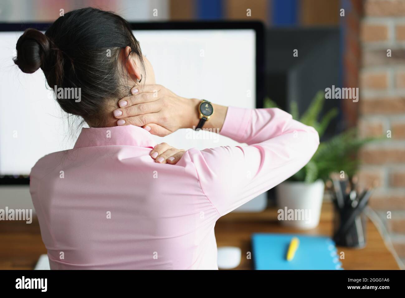 Young woman sitting at computer and holding her sore neck with her hand ...
