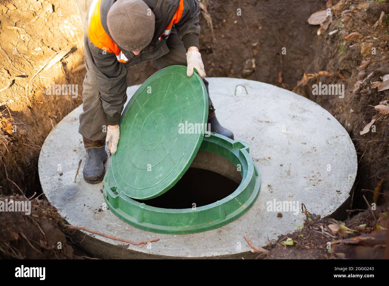 A worker installs a sewer manhole on a septic tank made of concrete ...
