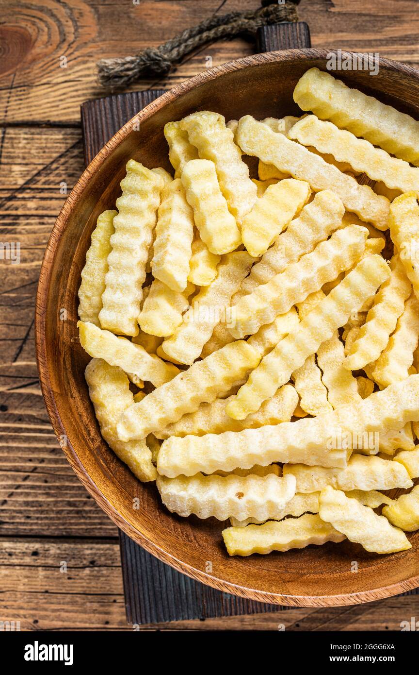 Cold Frozen Crinkle oven French fries potatoes sticks in a wooden plate ...