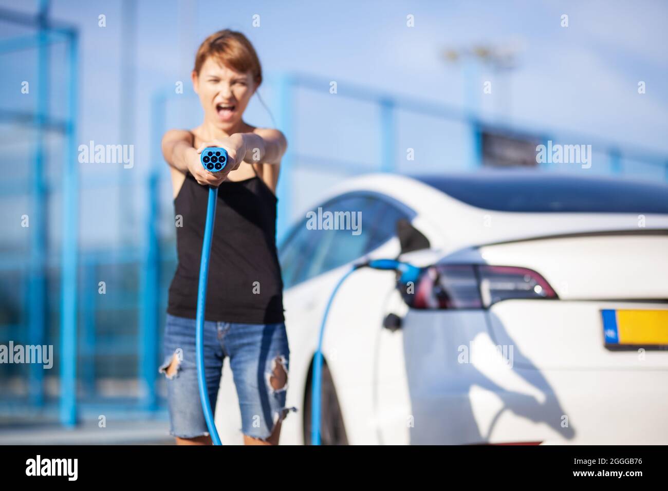 Beautiful young girl next to an electric car. Posing and holding a ...