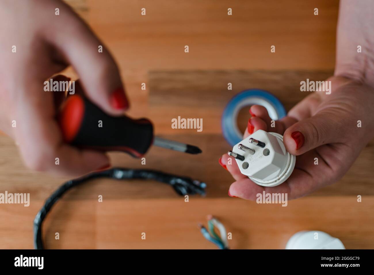 Overhead shot of a woman's hands repairing a plug using a screwdriver ...