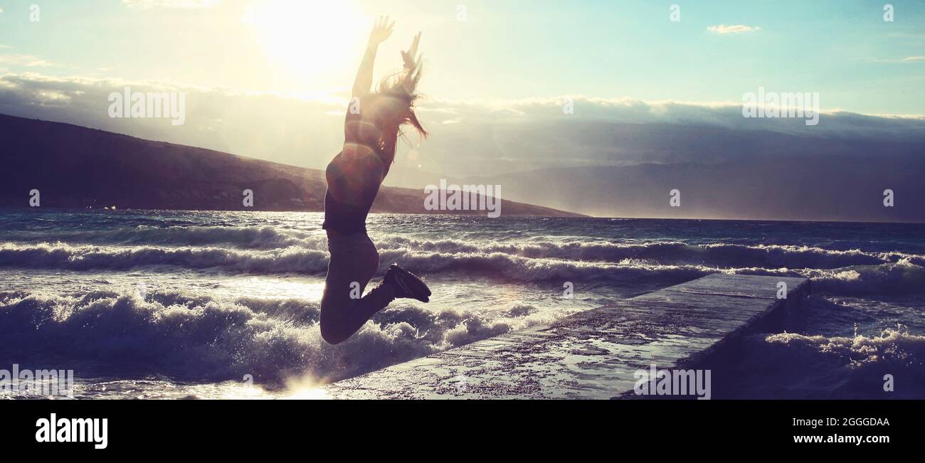 Feeling of freedom concept. Woman jump on pier facing to the sea with ...
