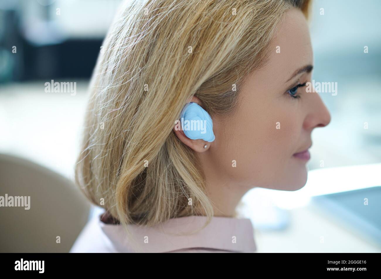 Pensive lady patient with a silicone earmold staring into the distance ...
