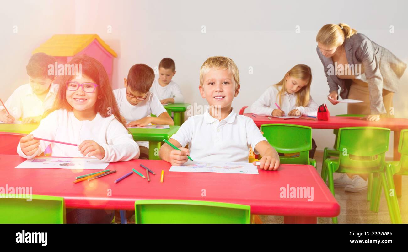 Female teacher helping schoolkids drawing with color pencils in ...