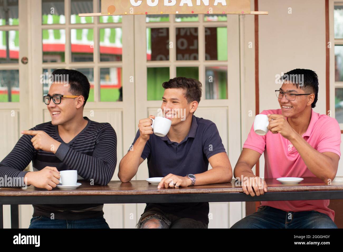 Three smiling students drinking at an outdoor latin cafe while looking ...