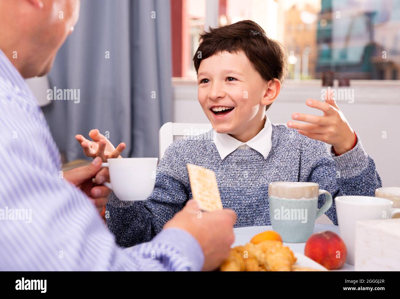 Son talking with father at table with tea during breakfast indoors ...