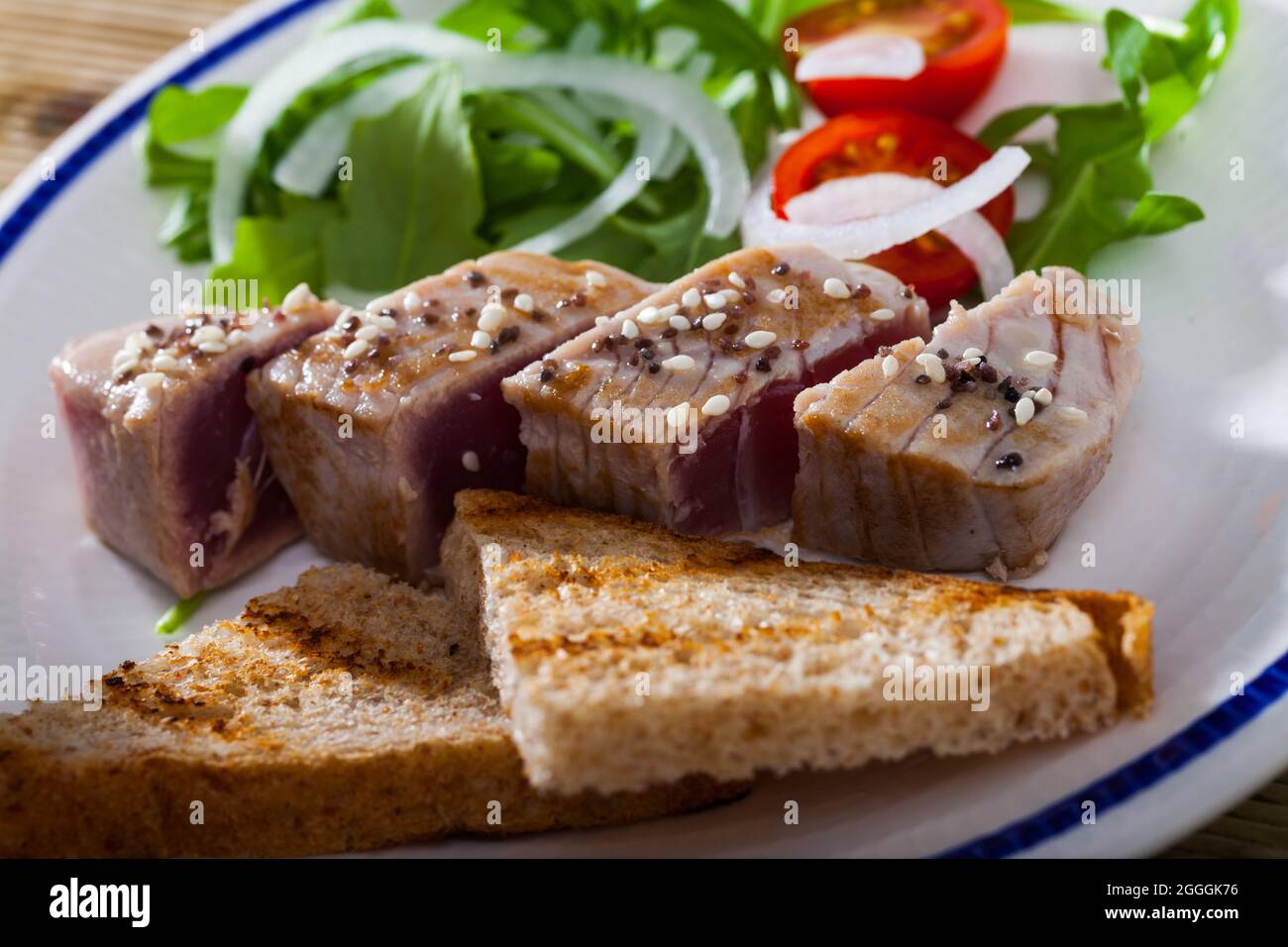 Tasty lightly fried tuna, served toasted bread and greens at plate ...