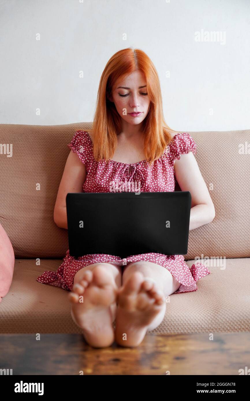 young woman using laptop working from home sitting on couch with feet ...