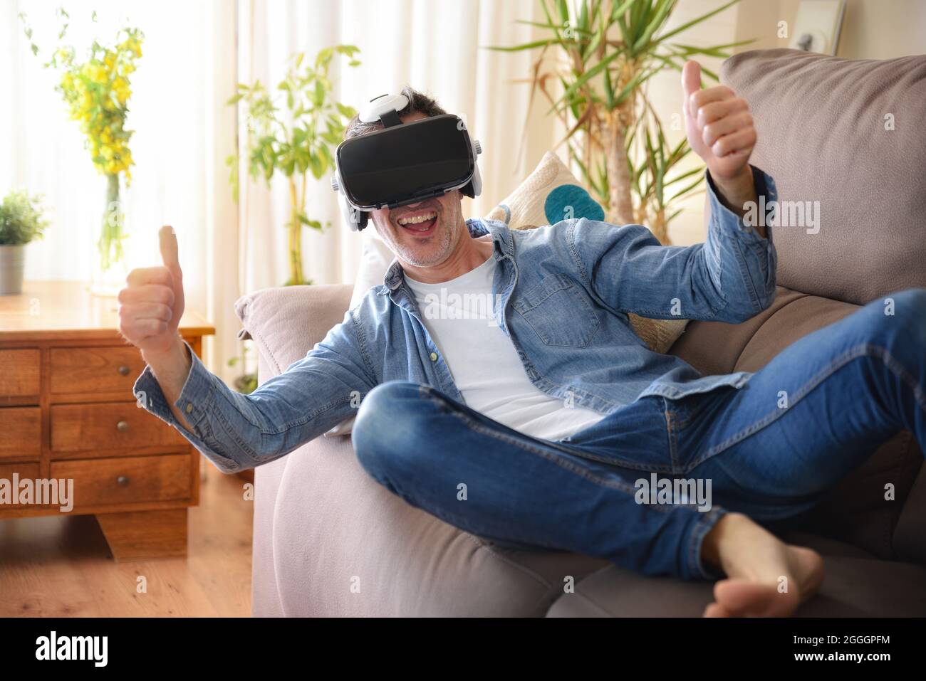 Happy entertaining man with virtual reality glasses lying on a sofa at ...