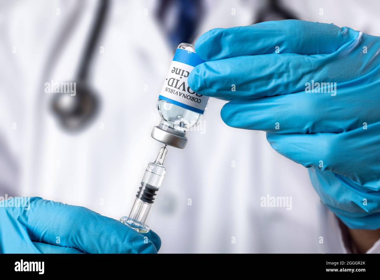 A doctor drawing liquid from a glass vial labelled covid-19 vaccine ...