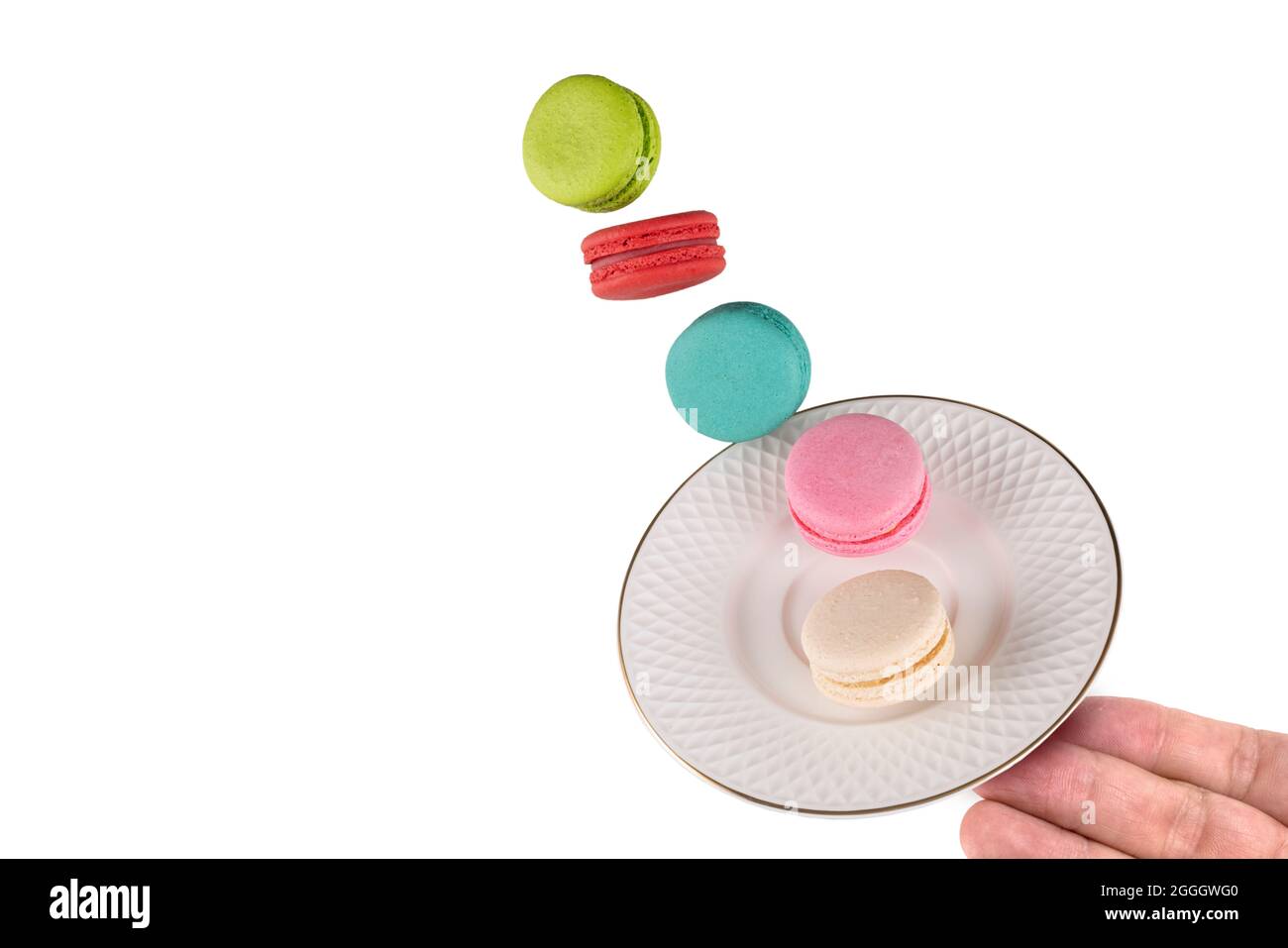 Colorful macaroons levitating on a white dinner plate held by a hand ...