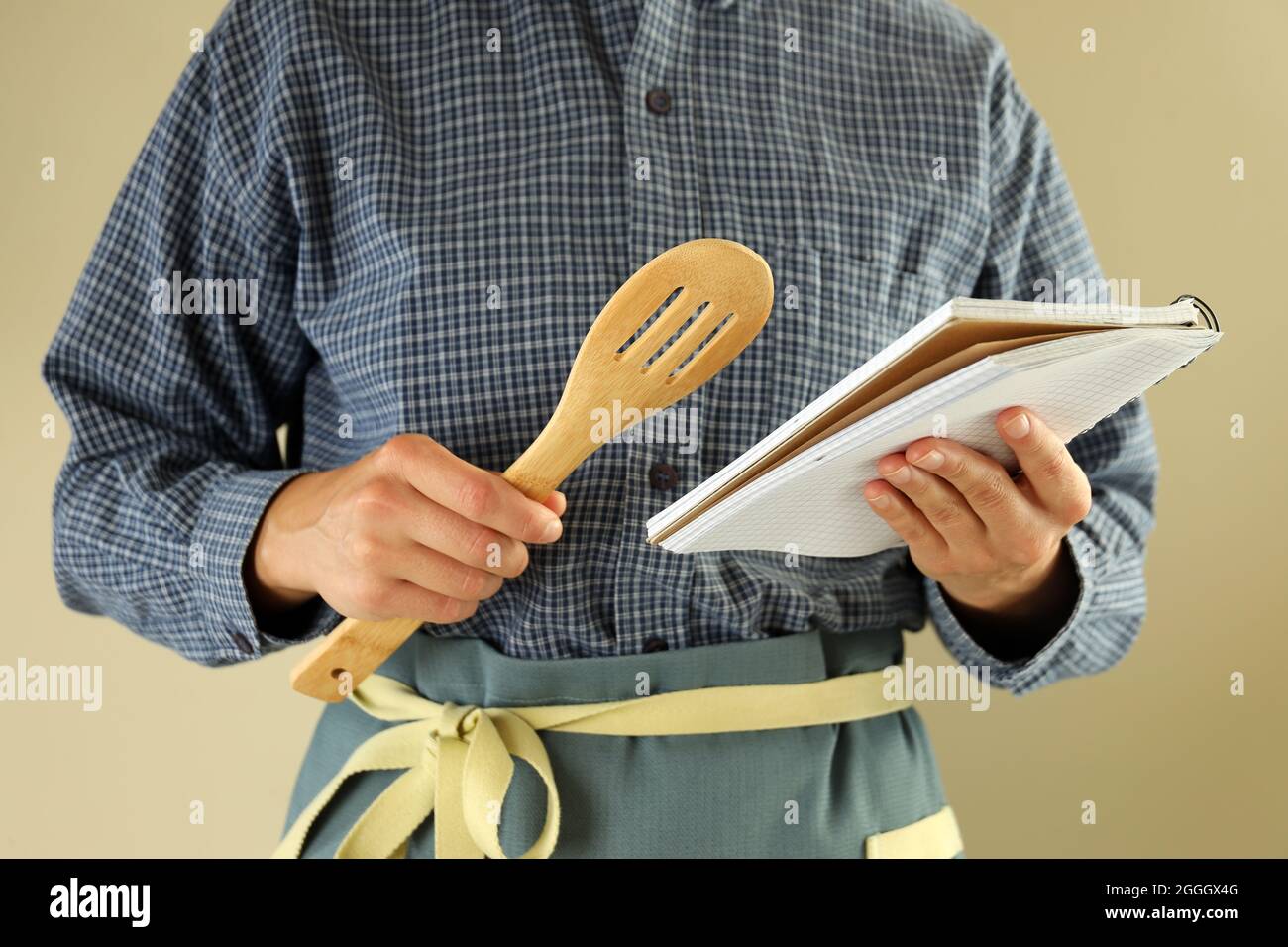 Woman holds recipe book and kitchen spatula on beige background Stock ...