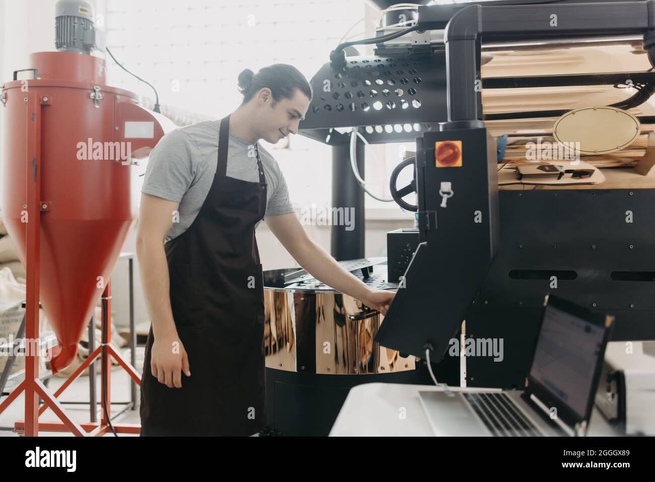 Attractive man in apron checking roasted coffee beans in cooling tray ...