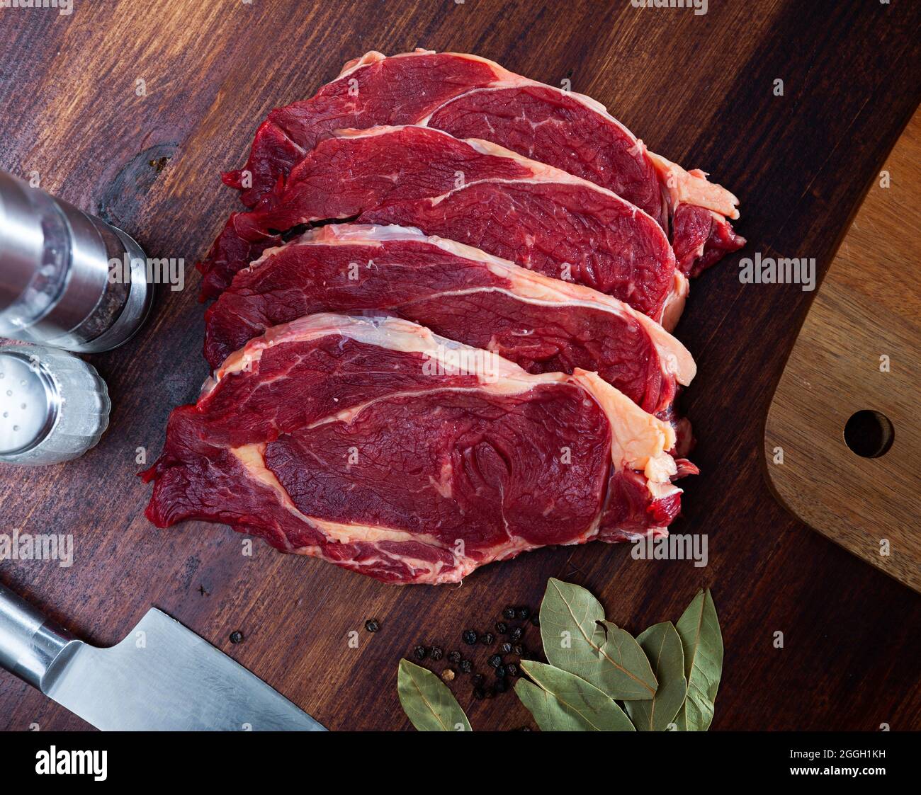 Sliced beef pieces on dark wooden board with laurel leafs and peas of ...