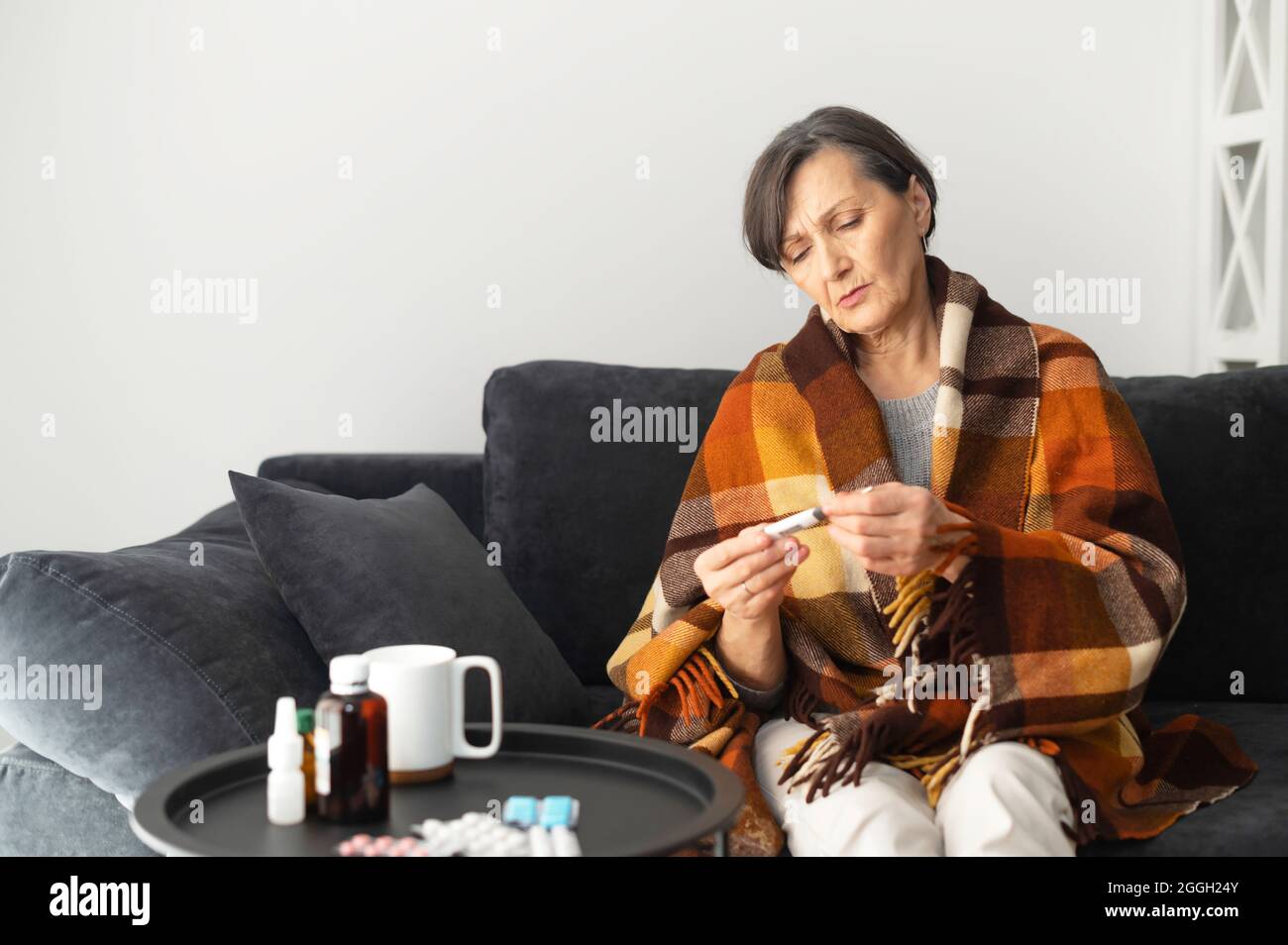 Senior woman feel sick, a mature older lady sits on the couch covered ...