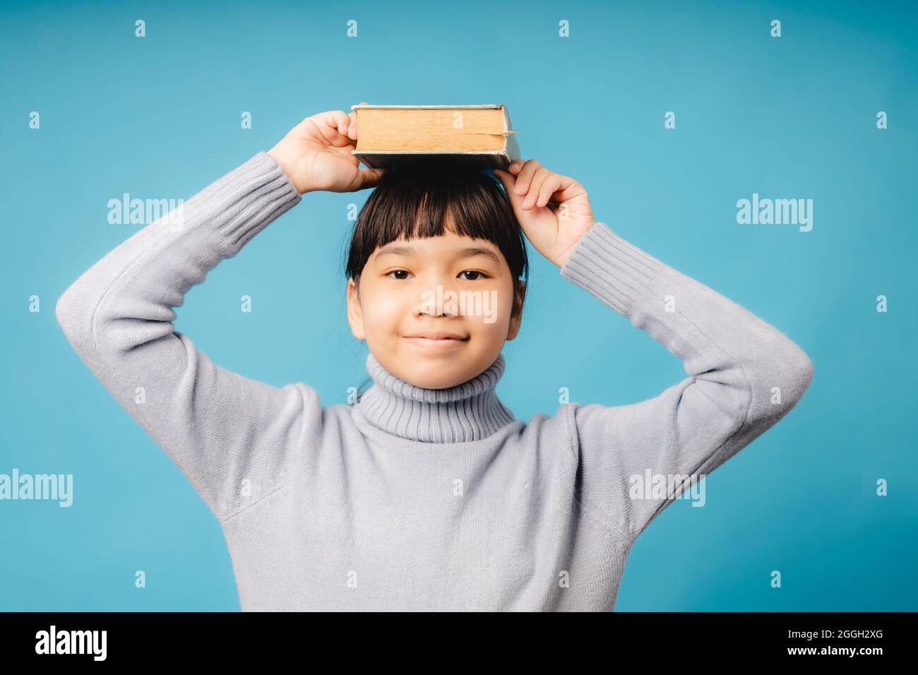 Asian girl kid holding text book on head of creative idea and bright ...