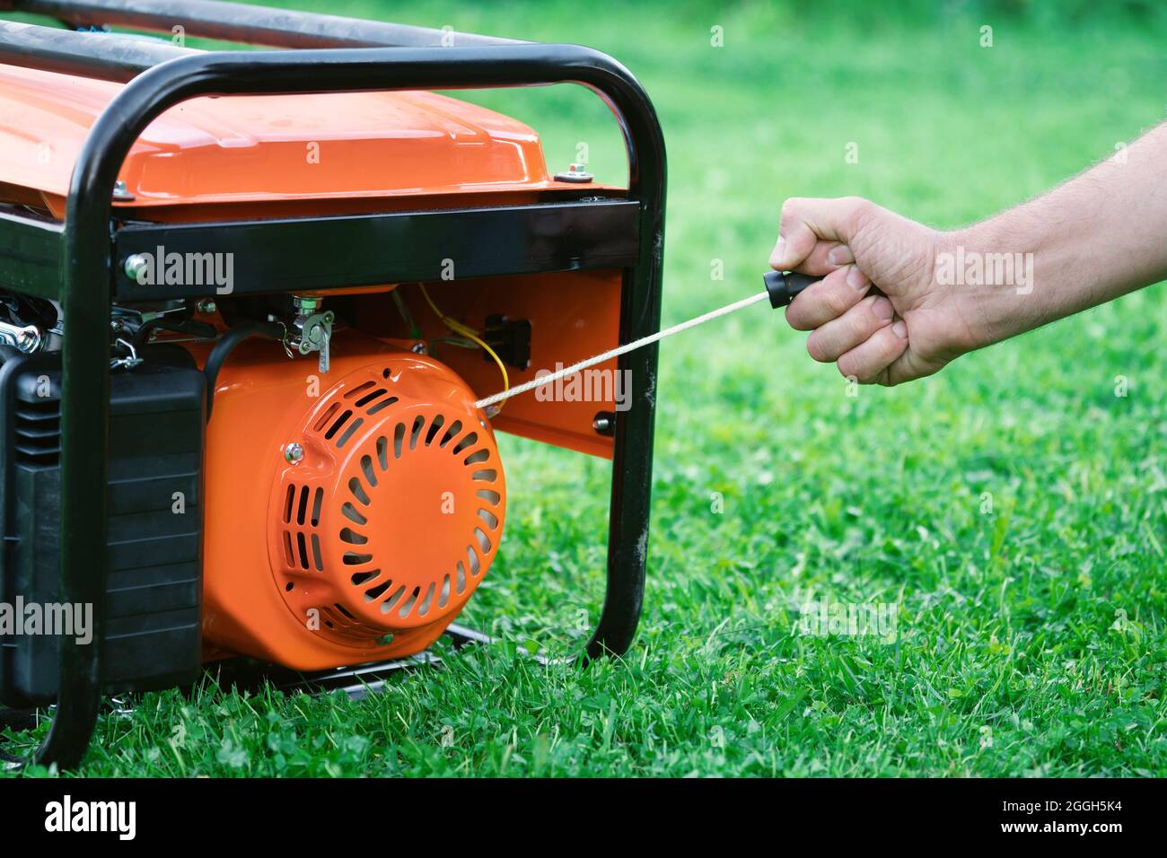 Hand starts a portable gasoline electric generator standing on the ...