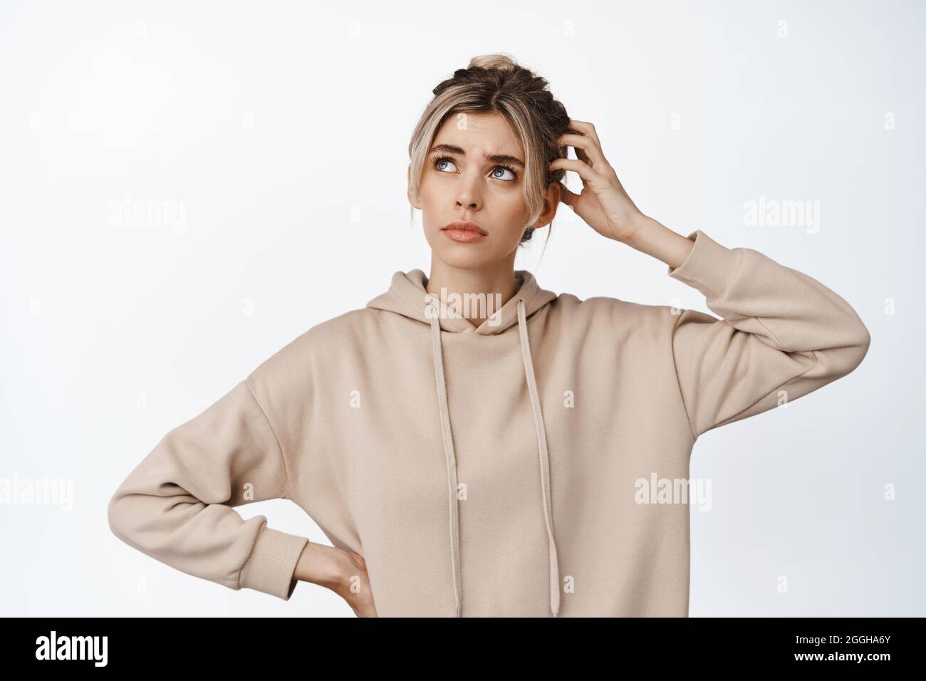 Puzzled young woman scratching head in doubt, looking up confused ...