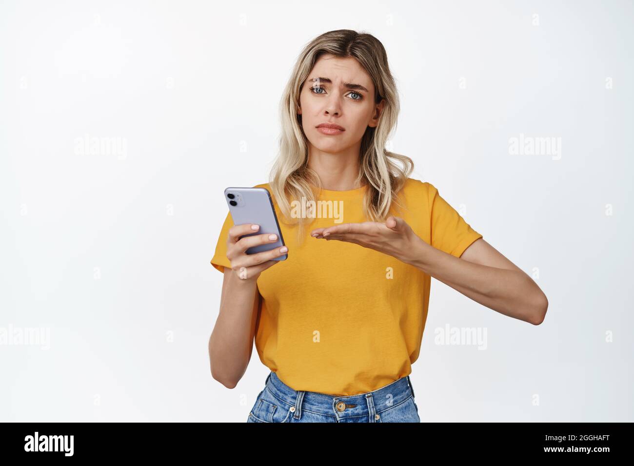 Troubled young woman asking help with mobile phone, pointing at ...
