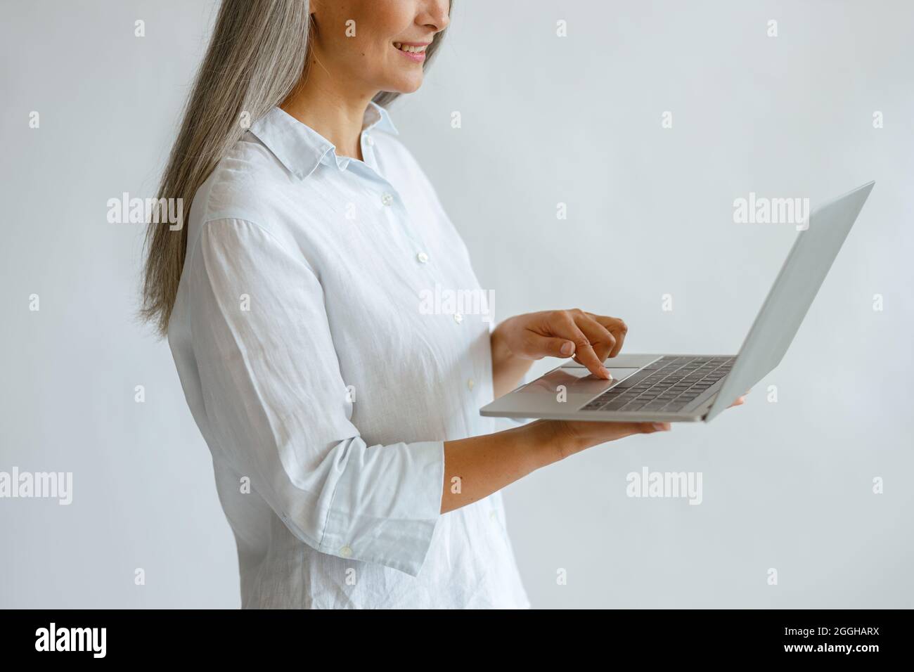 Hoary haired lady in white blouse uses laptop on light background in ...