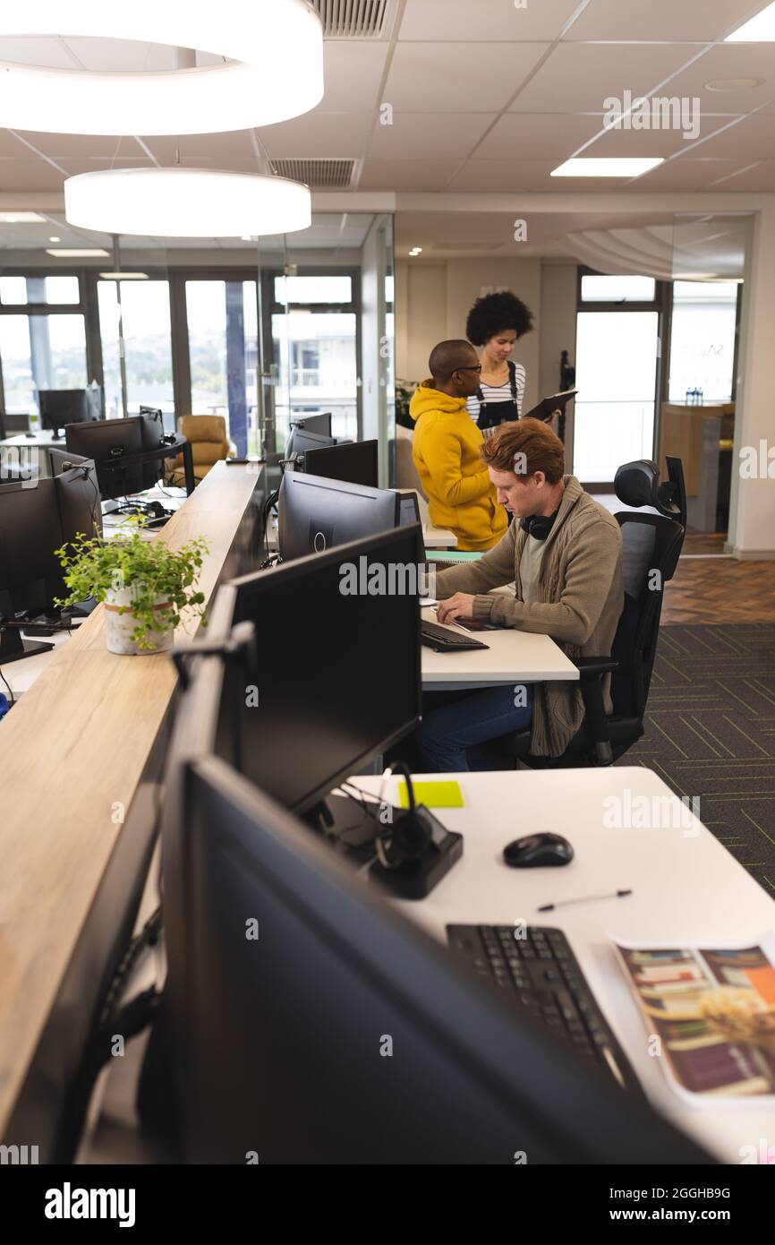 Diverse male and female colleagues at work, sitting at desks, using ...