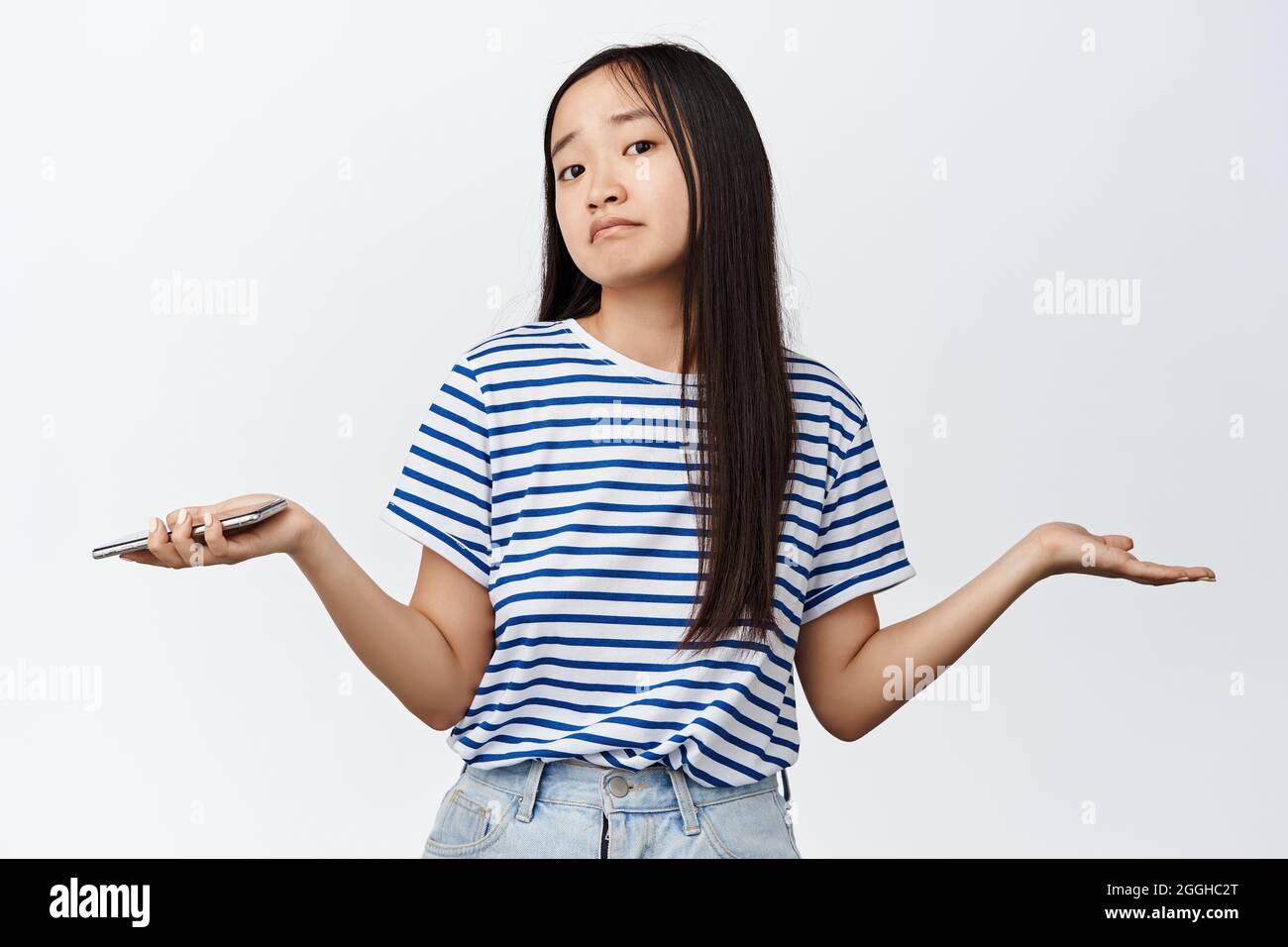 Confused asian girl shrugging shoulders while holding mobile phone ...