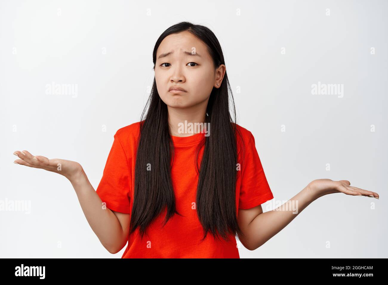 Puzzled asian girl shrugging, spread hands sideways and staring ...